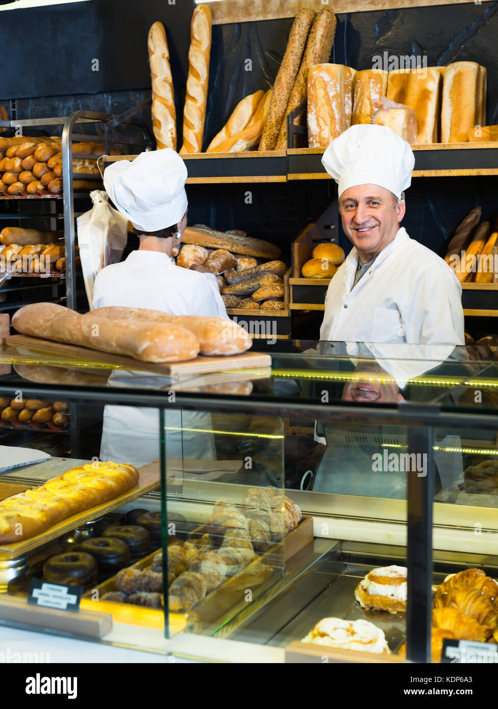 Bakery employees with tasty bread products on counter and shelves at ...