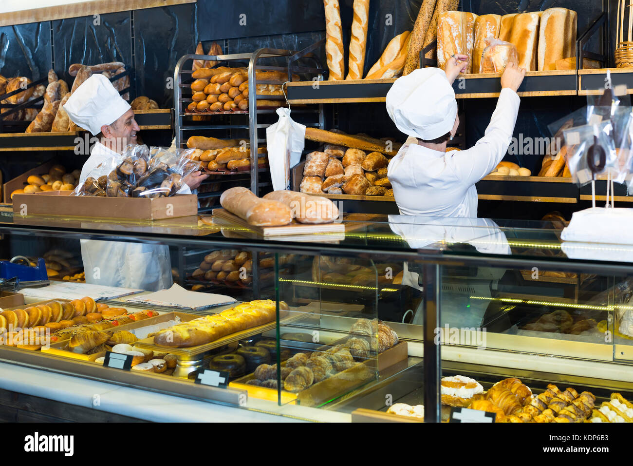 Two friendly smiling bakers at the counter with tasty bread products at ...