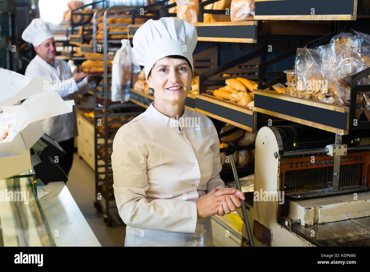 Portrait of cheerful female baker with fresh bread smiling in bakery ...