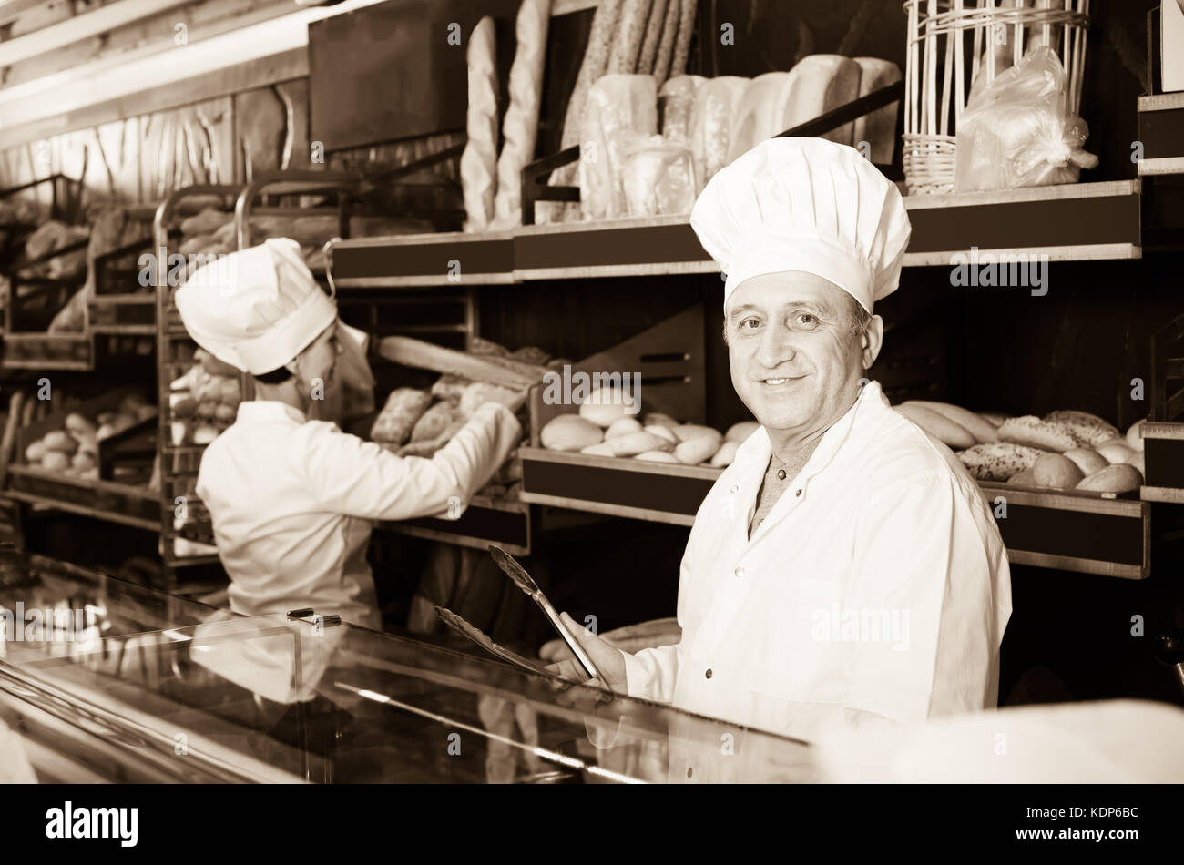 Portrait of joyous bakers with fresh bread smiling in bakery Stock ...