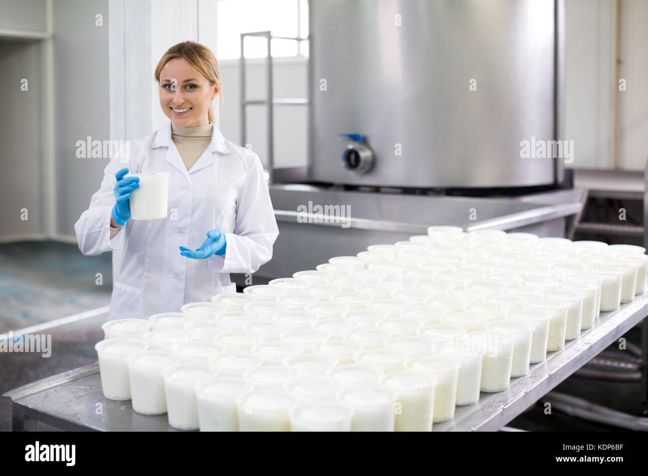 Smiling woman wearing uniform showing cottage cheese production process ...