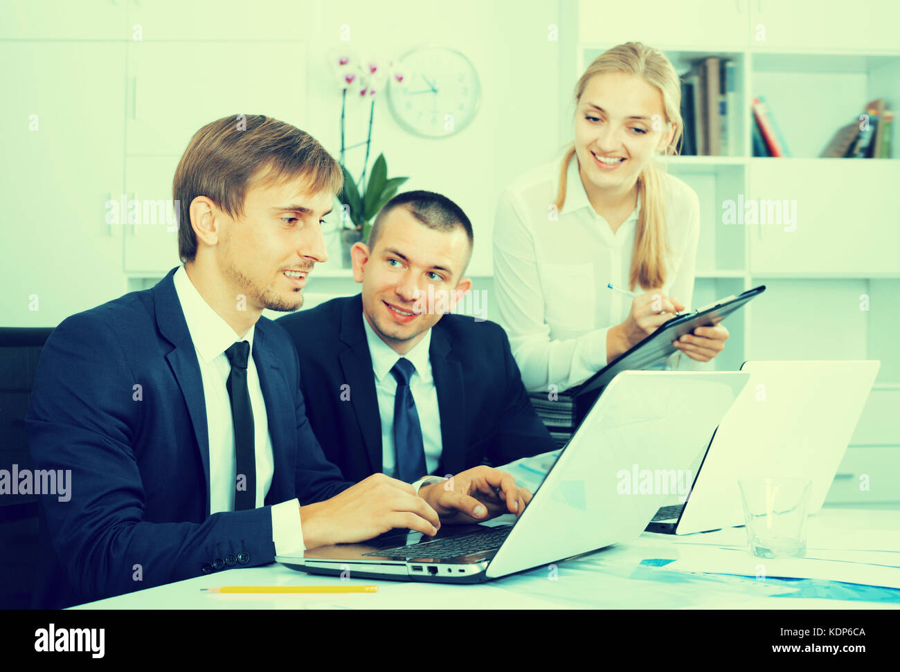 Two glad business male assistants working using laptops and woman with ...