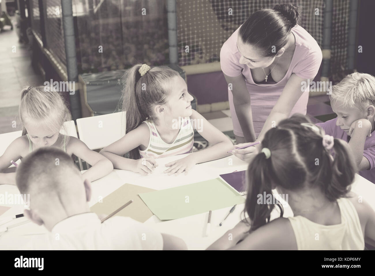 Glad children drawing on lesson in elementary classroom with help of ...