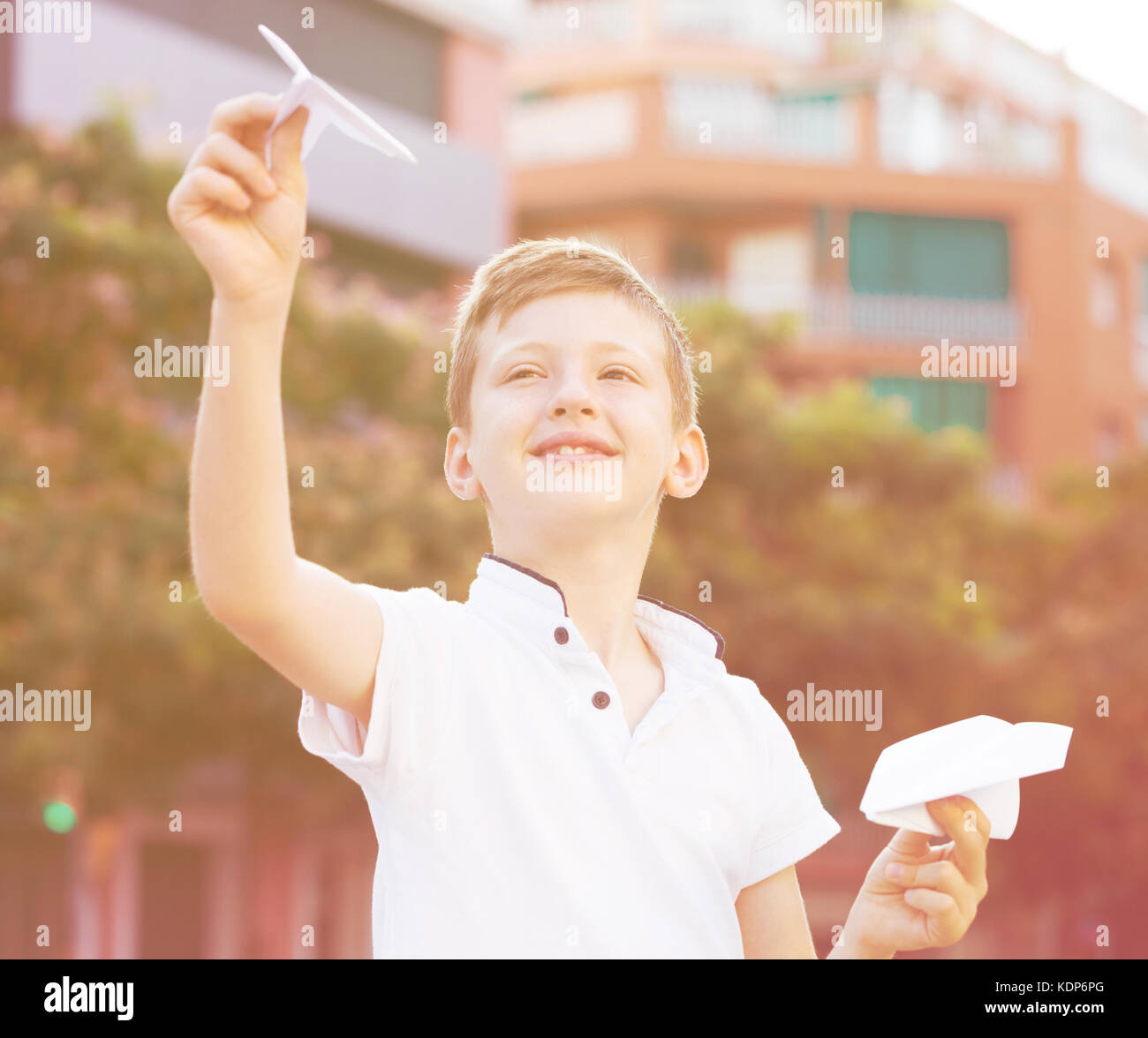 portrait of glad boy throwing paper airplanes in park on summer day ...