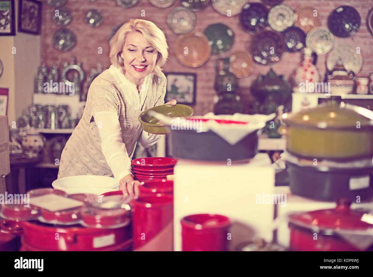 Portrait of happy blonde woman chooses ceramic ware in the cookware ...