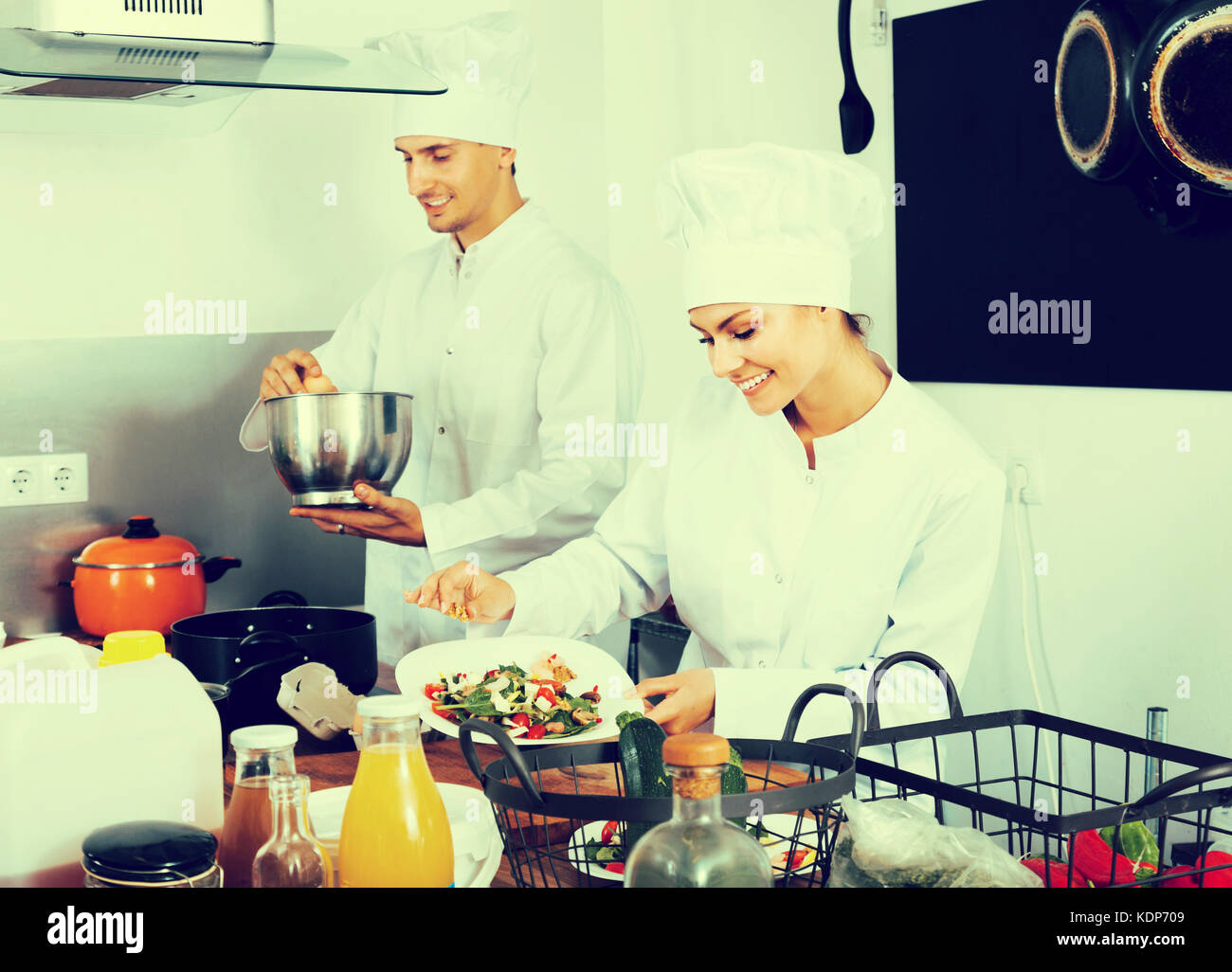 Two pretty young man and woman chefs cooking food at restaurant's ...