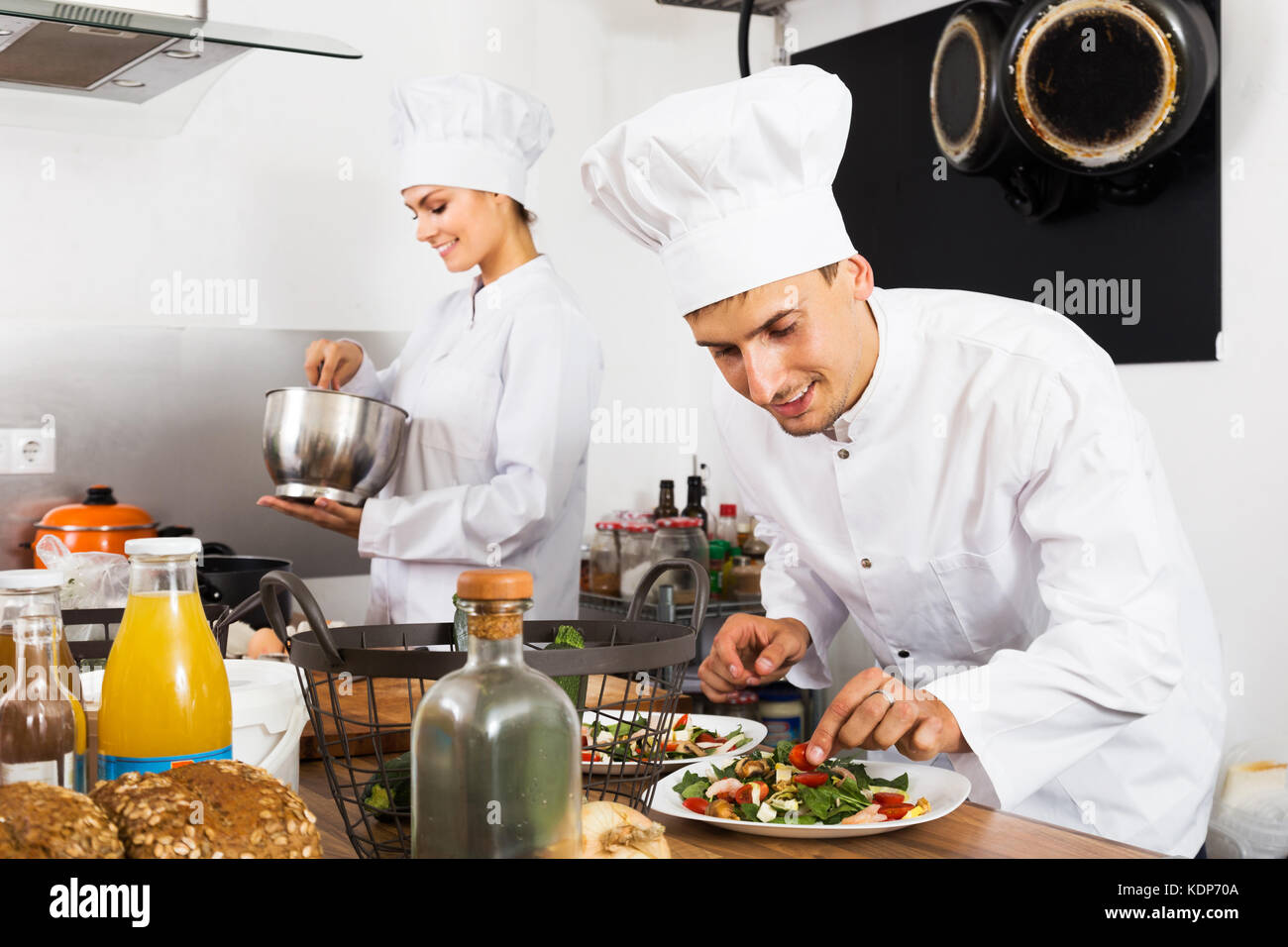 Two young man and woman chefs cooking food at restaurant's kitchen ...