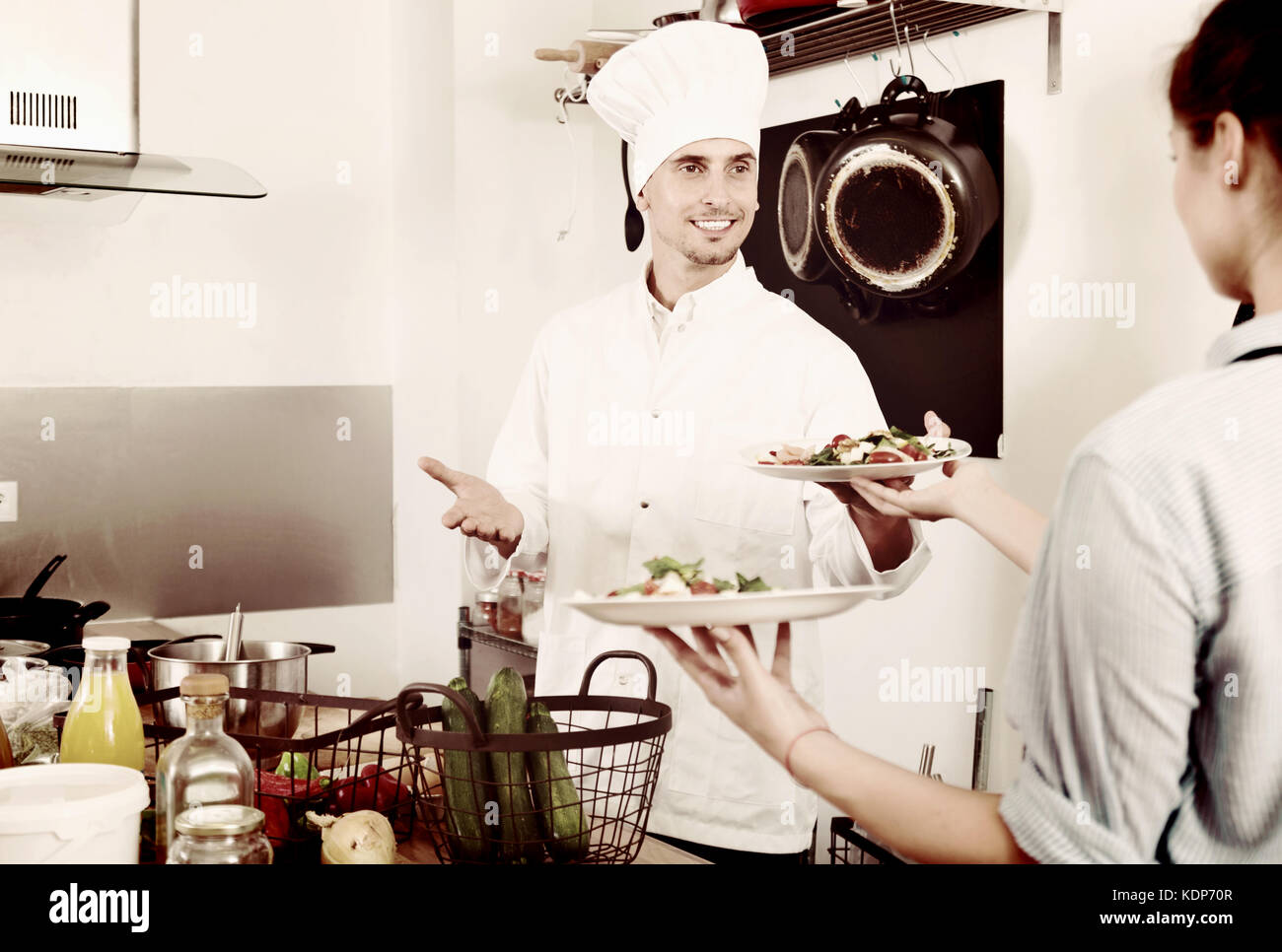 Portrait of young smiling man cook giving to waitress ready to serve ...