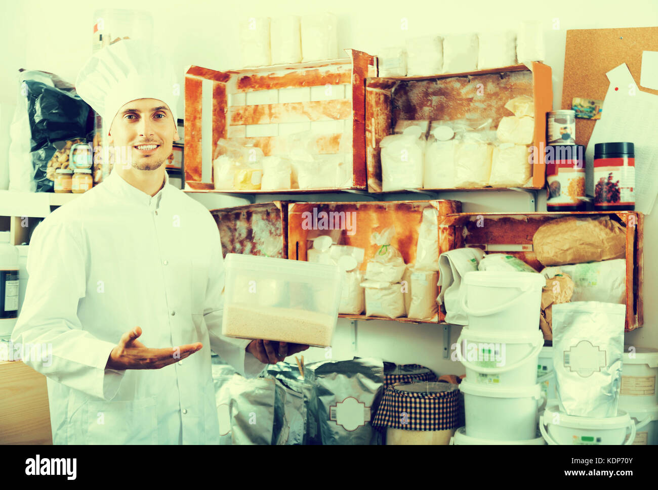 Cheerful man chef wearing uniform holding various flour in rooms with ...