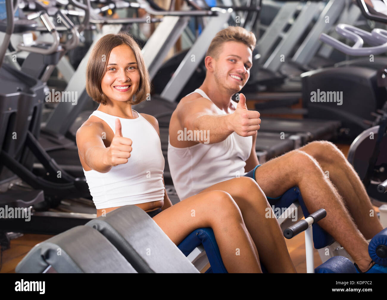 young american man and woman making sit ups together using machine in ...