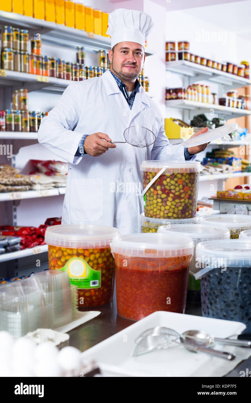 smiling salesman offering salted olives with filling in ordinary food ...