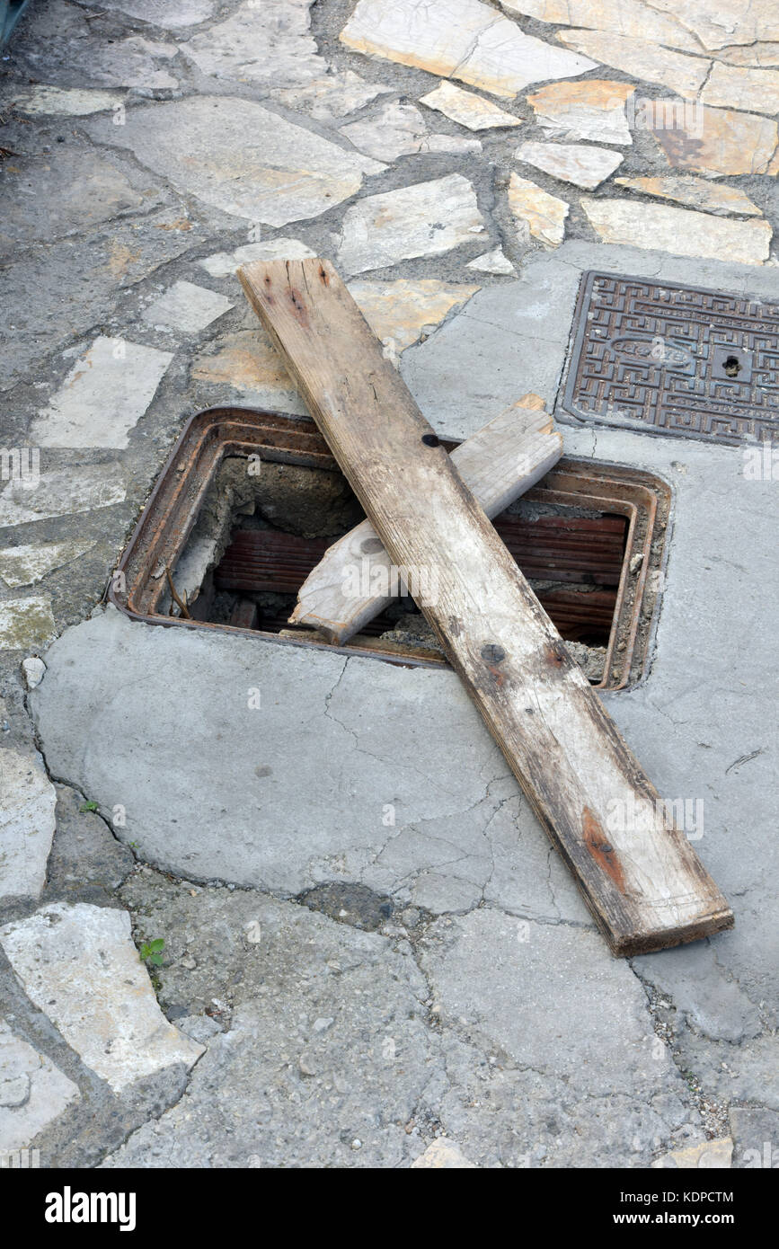 A missing manhole cover on a pavement in Greece covered by two planks ...