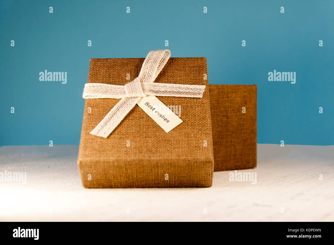 A brown gift box and a beige ribbon with a tag on a light background. A ...