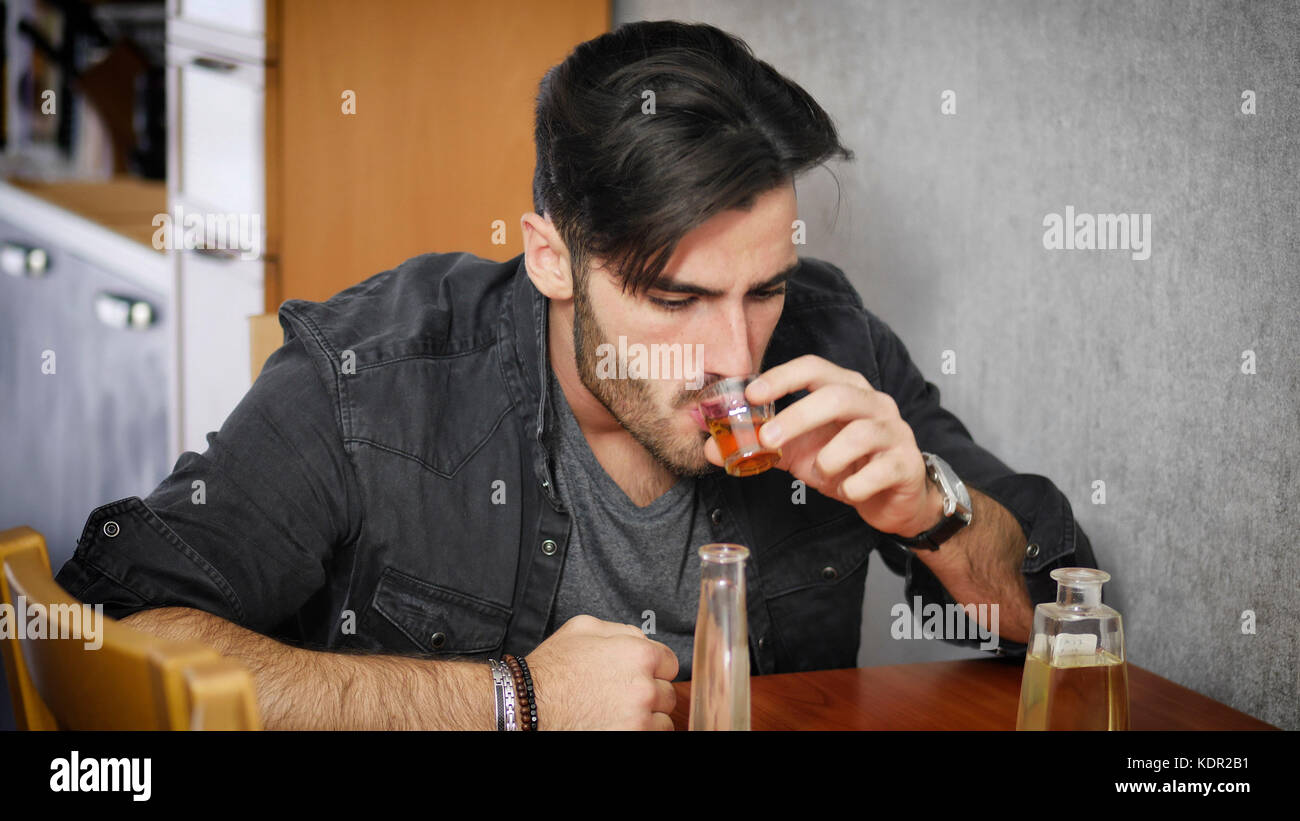 Young man sitting drinking alone at a table with two bottles of liquor ...