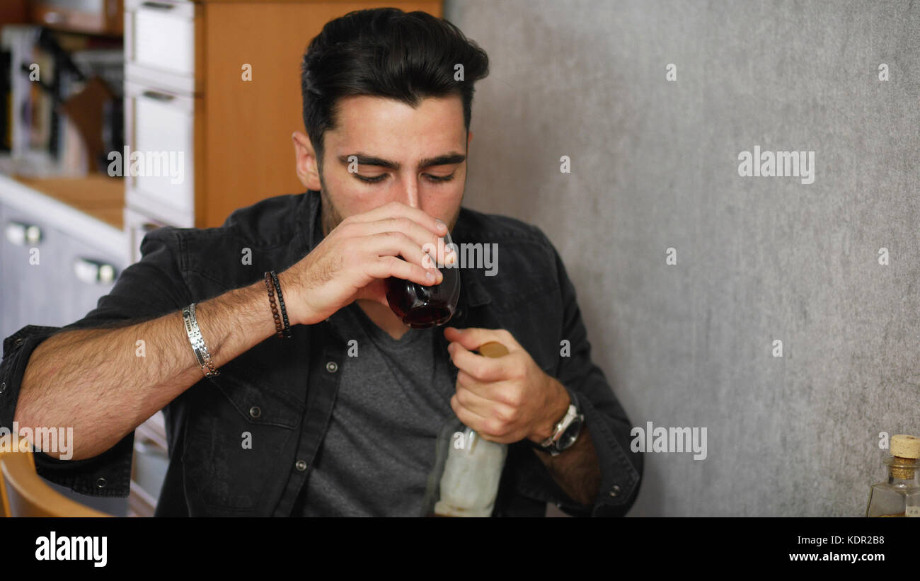 Young man sitting drinking alone at a table with two bottles of liquor ...