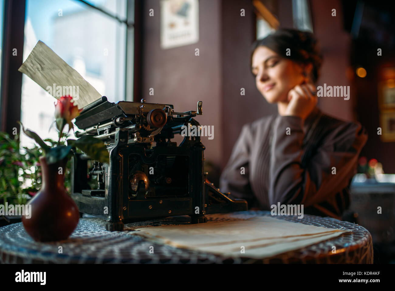 Smiling dark hair lady sits by table with ancient typewriter. Portrait ...