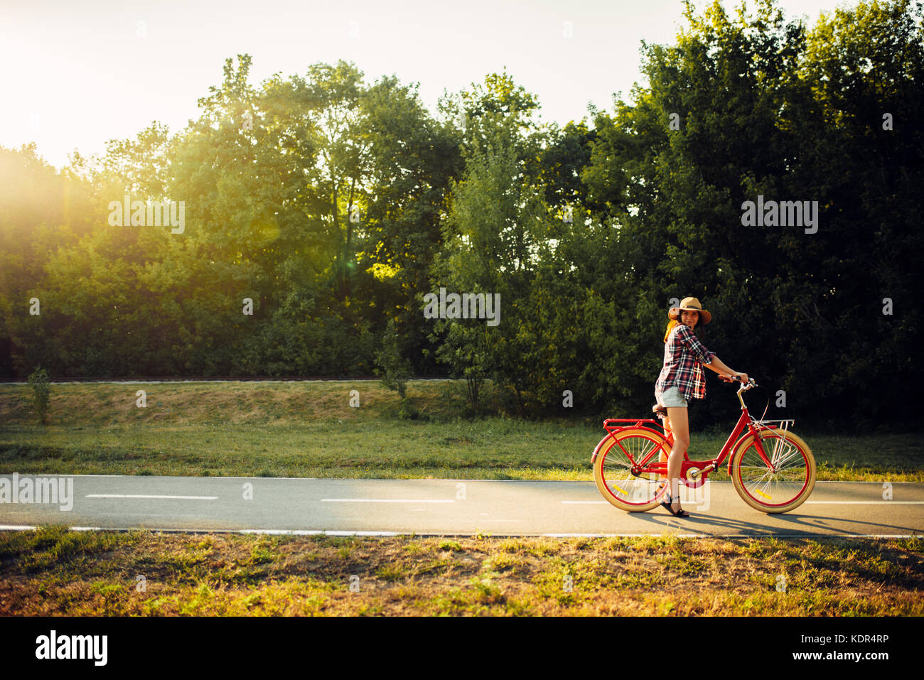 Young woman riding on red vintage bicycle in summer park on sunset ...