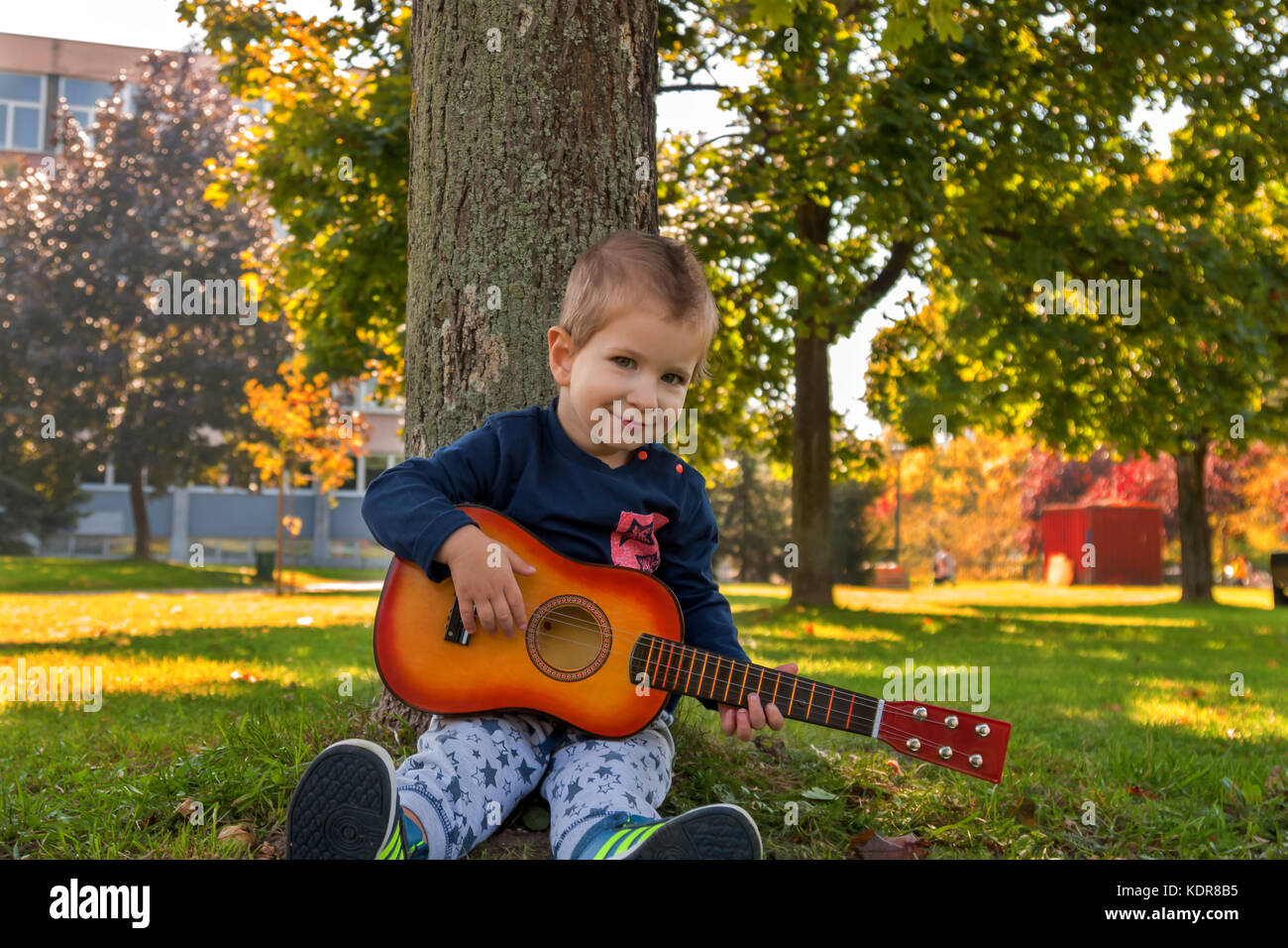 Small boy holding acoustic guitar while sitting leaned on a tree Stock ...