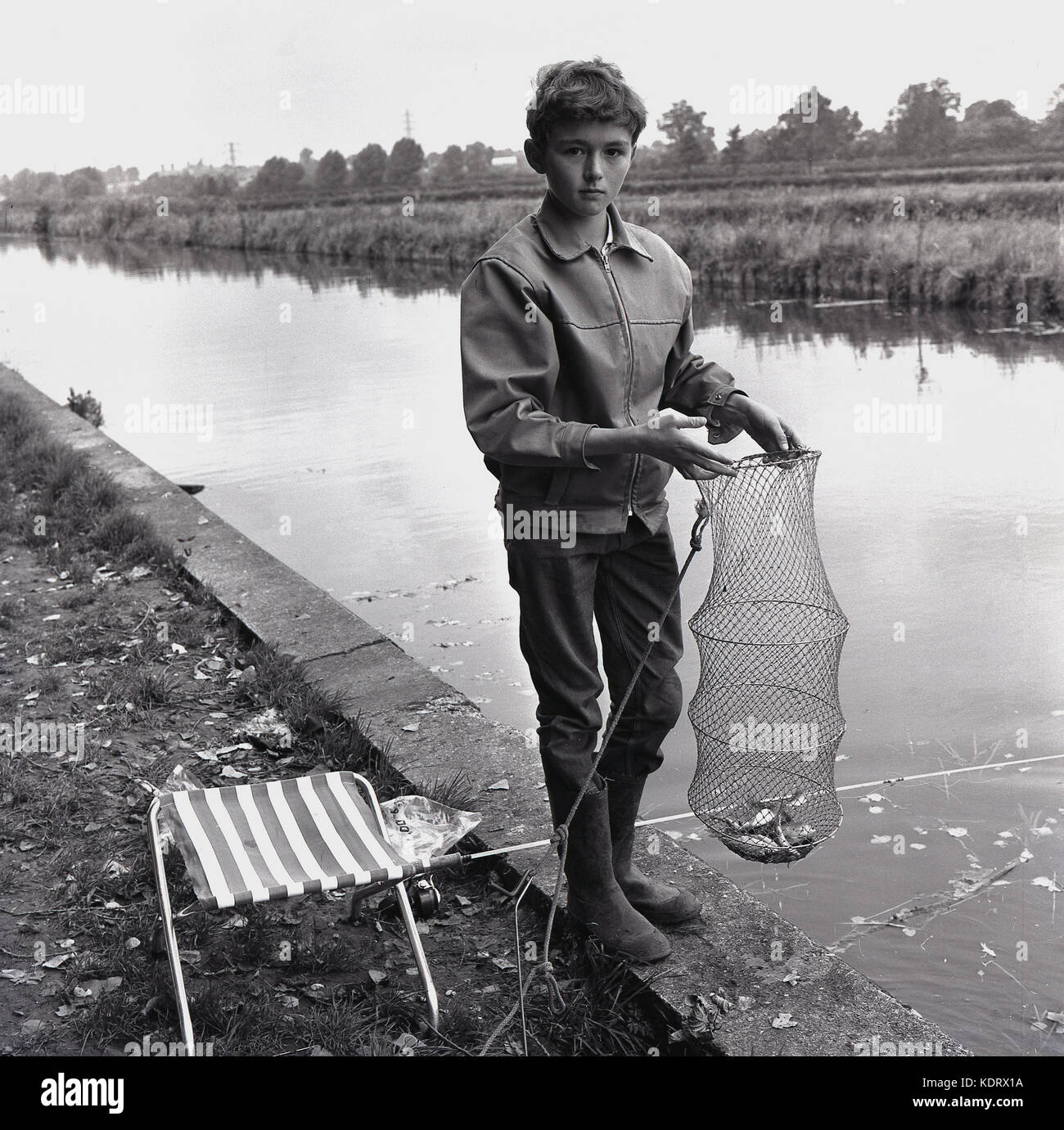 1960s, historical, young boy fishing beside a canal, shows his catch in ...