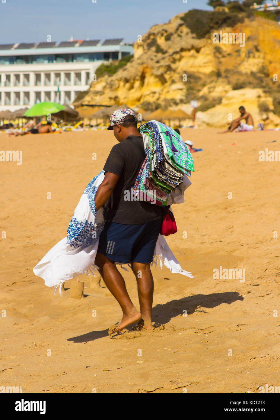 A beach trader carrying his stock of colourful fabrics along the beach ...