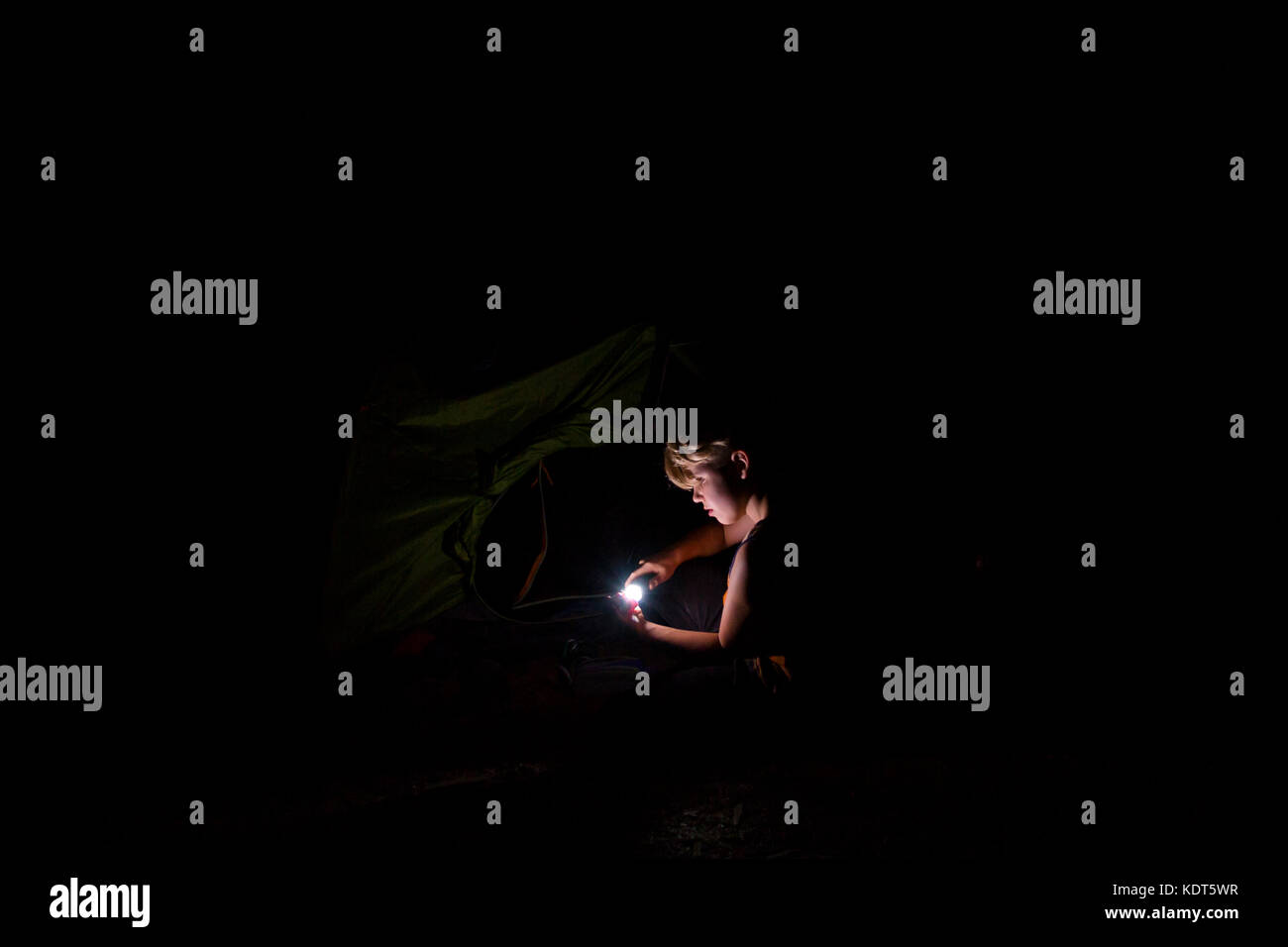 A boy plays with a flashlight, illuminating his face and pushing back ...