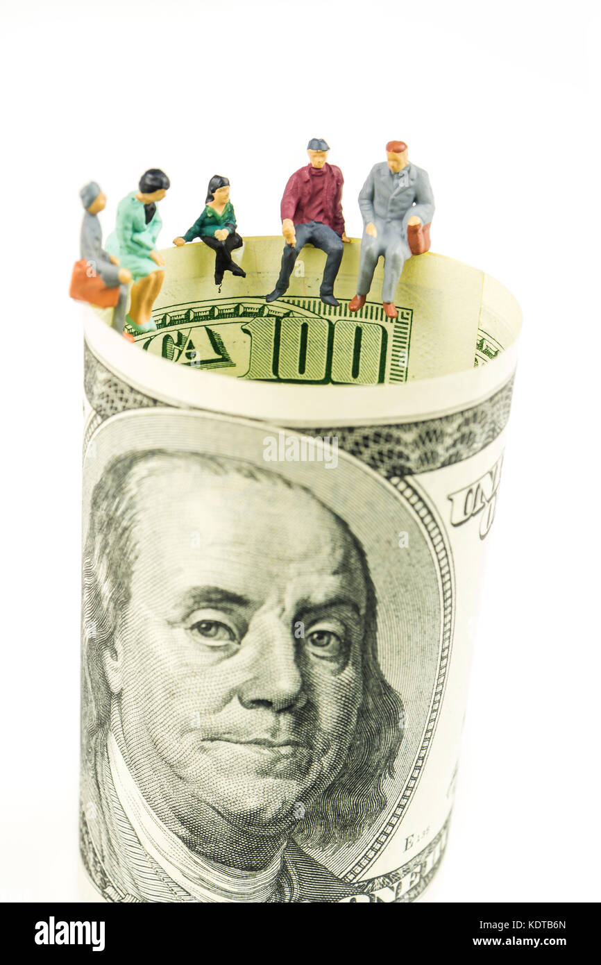 miniature figurines sitting on the edge of 100 rolled up dollar ...