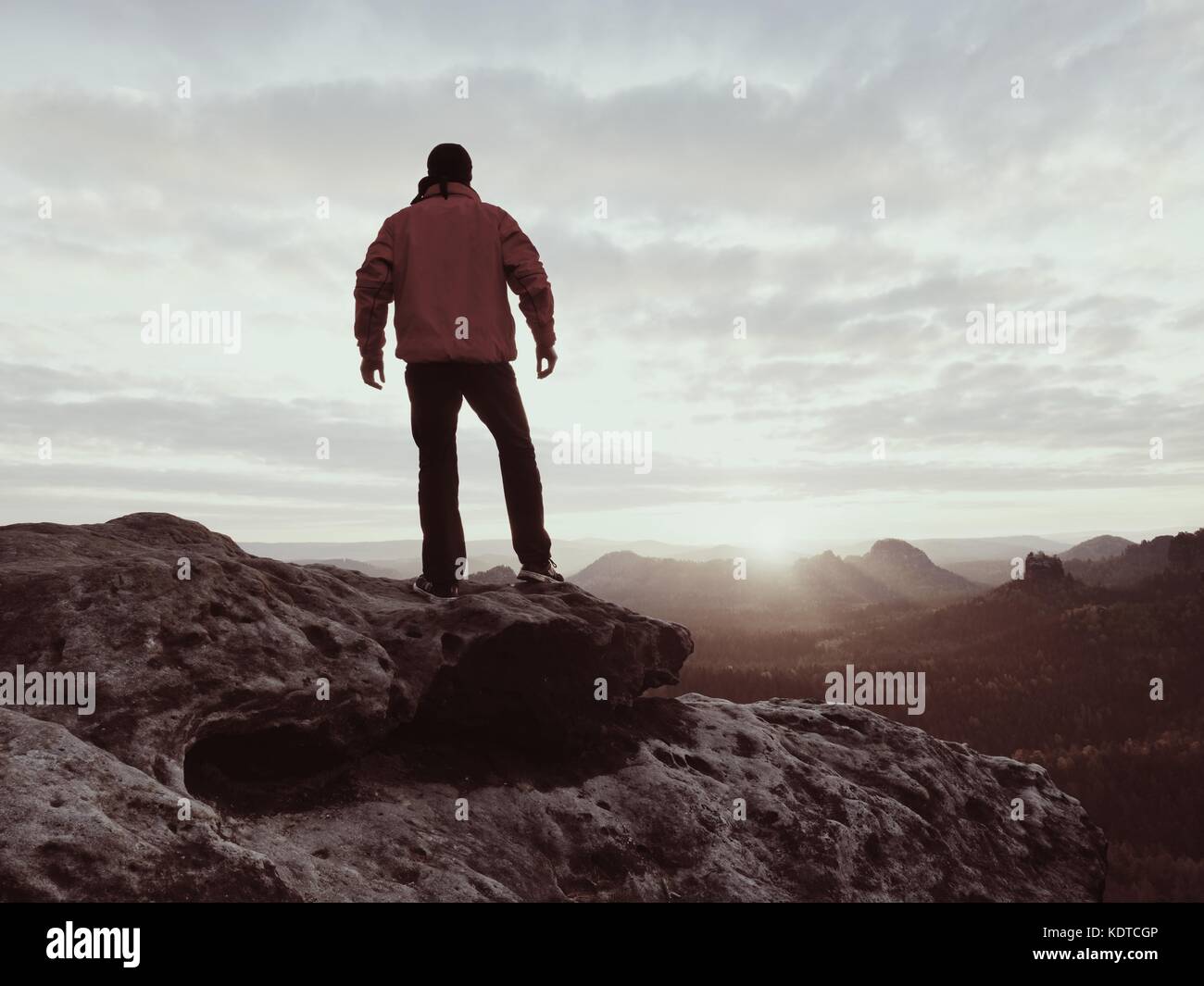 Alone tourist with cap and sporty outdoor clothes stand on cliff edge ...