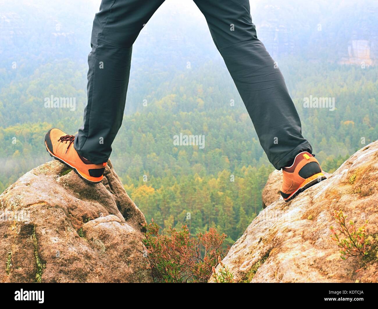 Male legs in dark hiking trousers and leather trekking shoes on peak of ...
