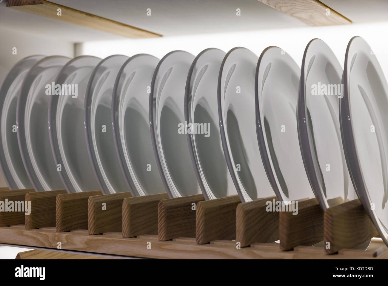 Ceramic white plates on wooden shelf in a row closeup Stock Photo - Alamy