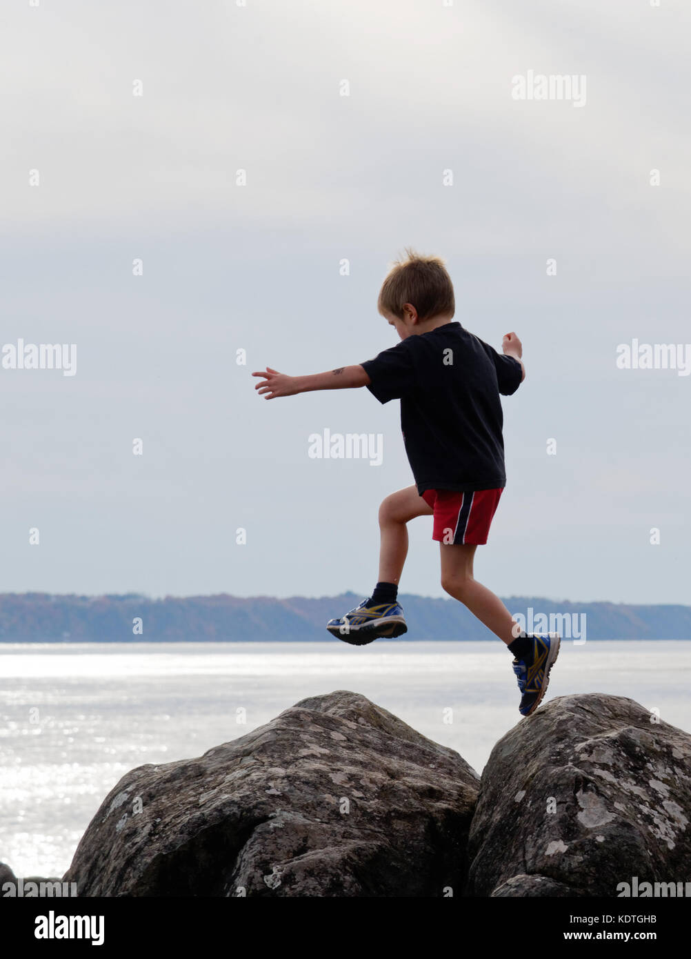 A little boy (5 yrs old) leaping across rocks on the shore of the St ...