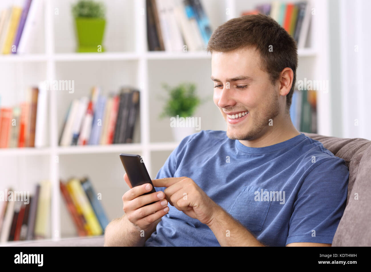 Happy guy using a smart phone on line sitting on a sofa at home Stock ...