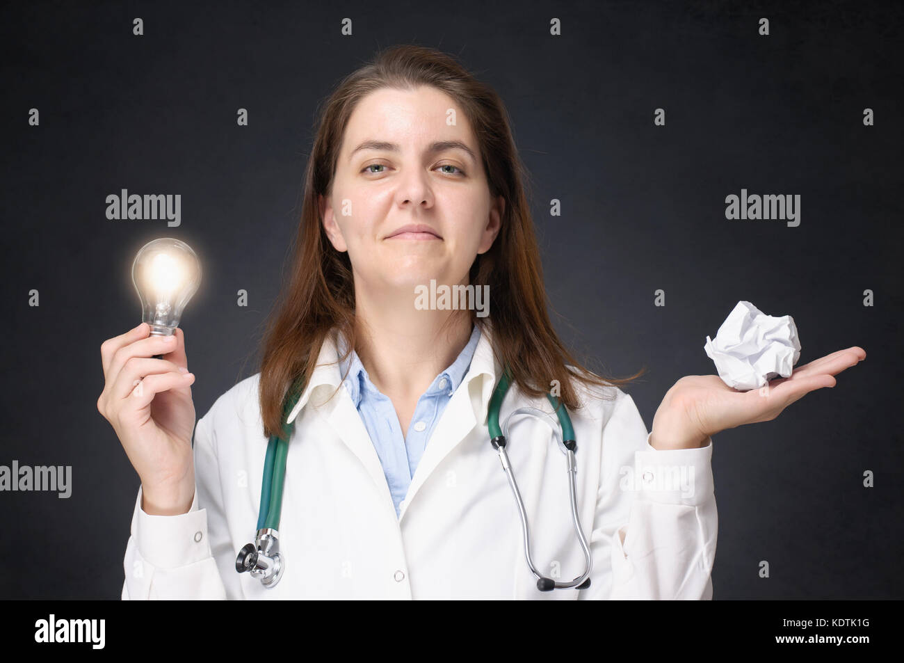Female doctor holding a glowing light bulb and a crumpled paper ball ...