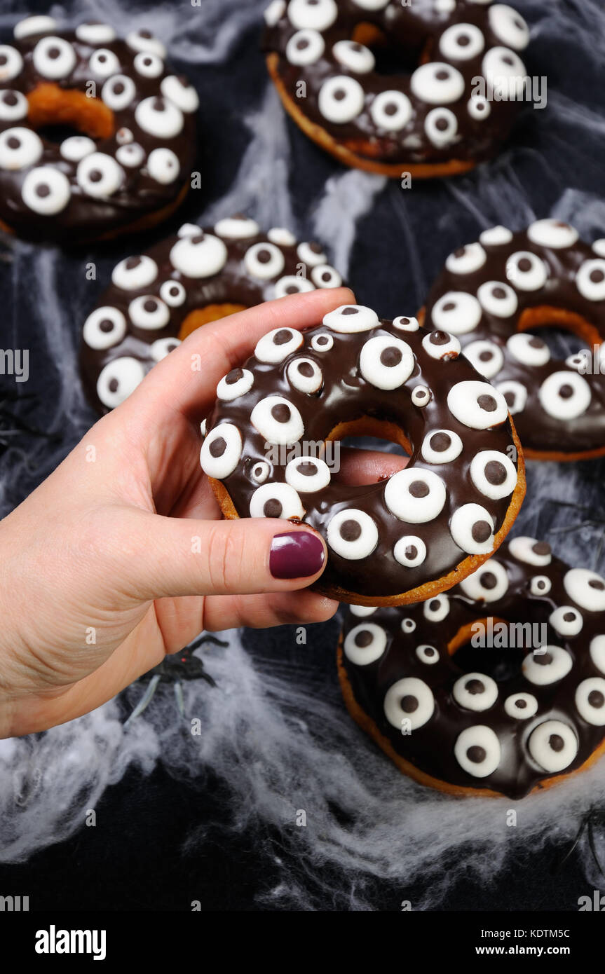 Hand holds a donut with chocolate icing decorated googly eyes on ...