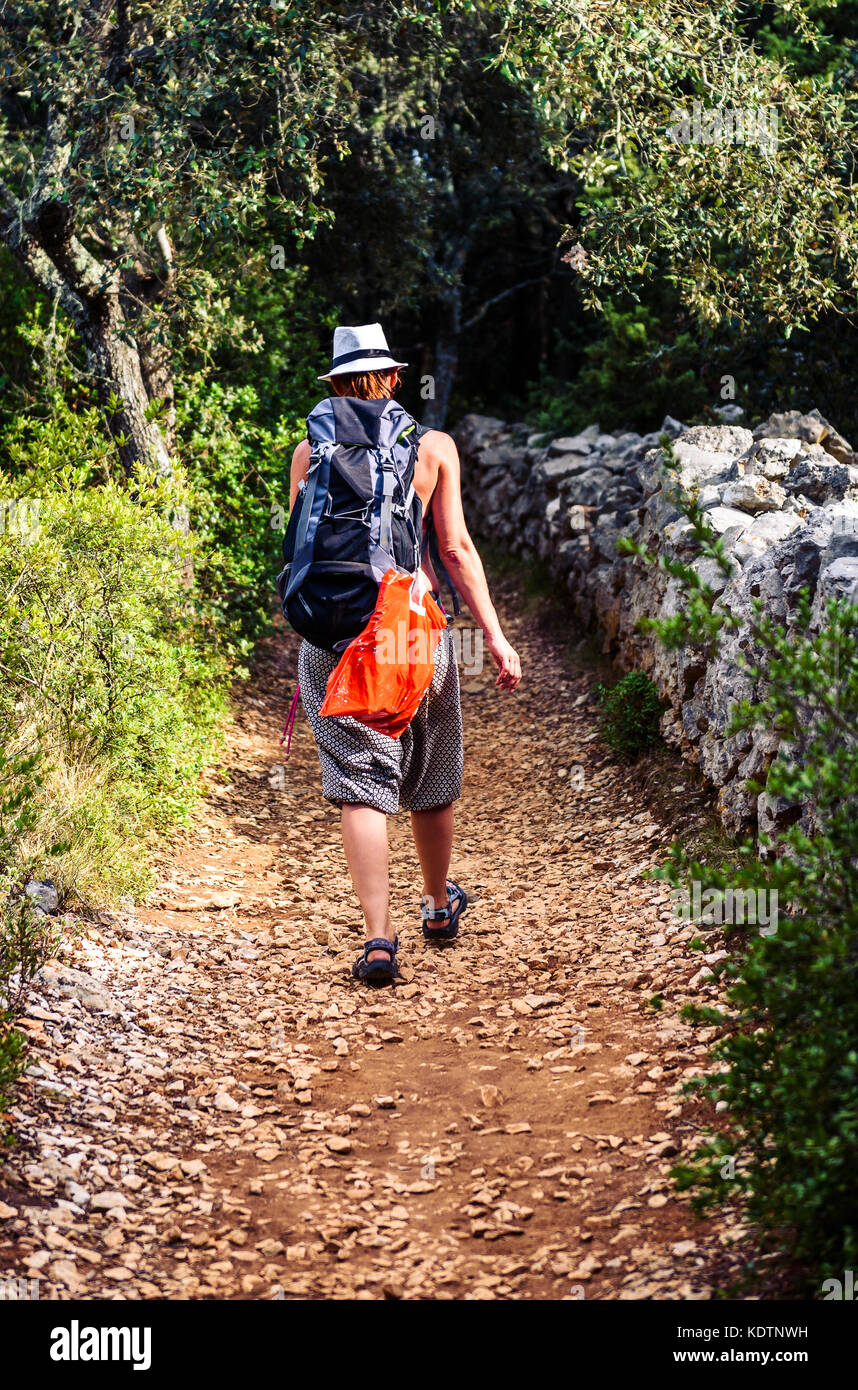 Woman hiking on country footpath with rock fence and woods. Hiker with ...