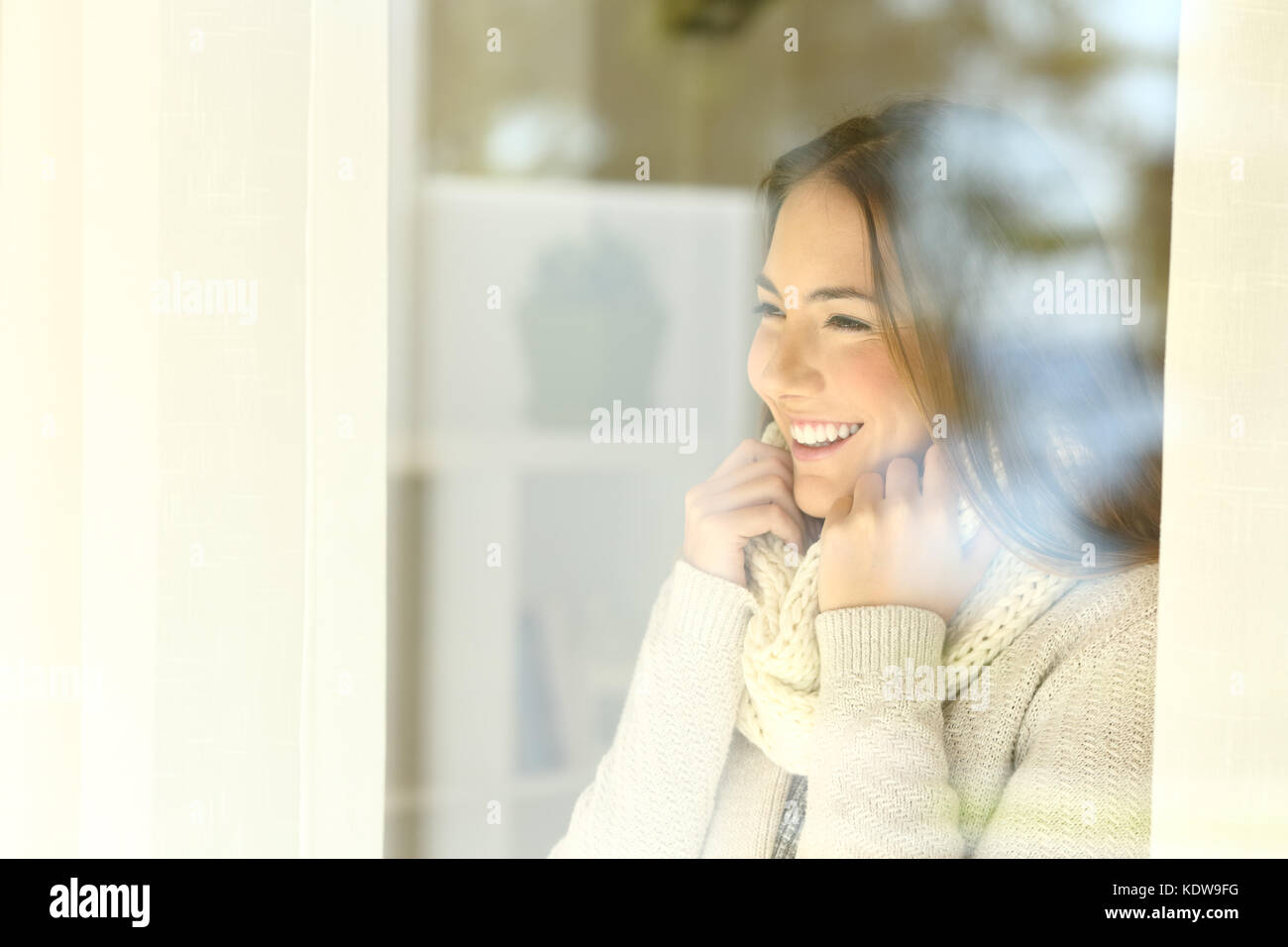 Happy woman warmly clothed looking outside through a window in winter ...