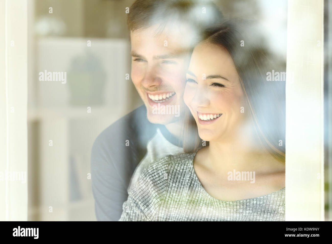 Portrait of a happy couple in love looking through a window at home or ...