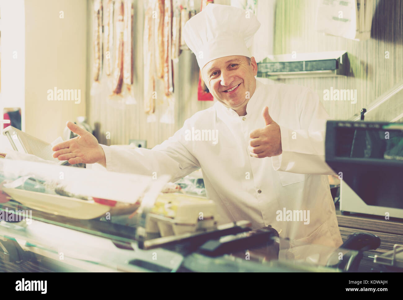 Mature male butcher with wurst and smoked meat at counter Stock Photo ...
