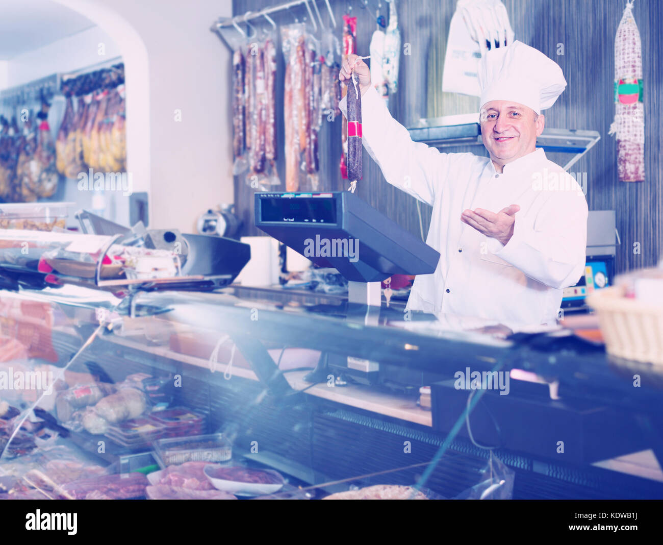 Mature male butcher with ham and smoked meat at counter Stock Photo - Alamy