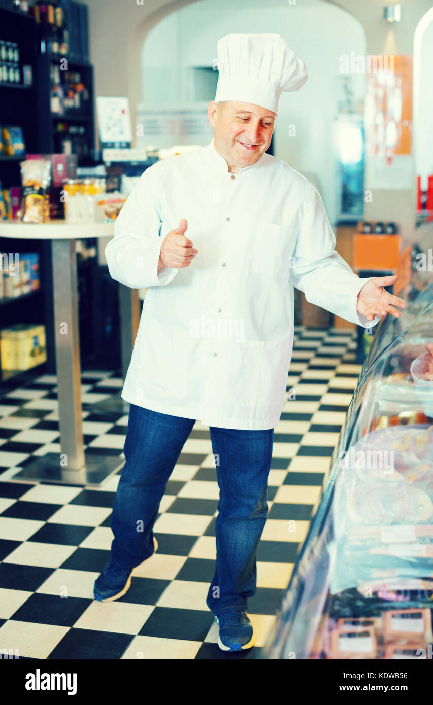 elderly male butcher with wurst and smoked meat at counter Stock Photo ...
