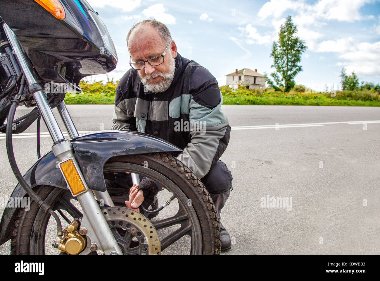 elderly man checking his motorcycle's wheel outdoor on the road on ...
