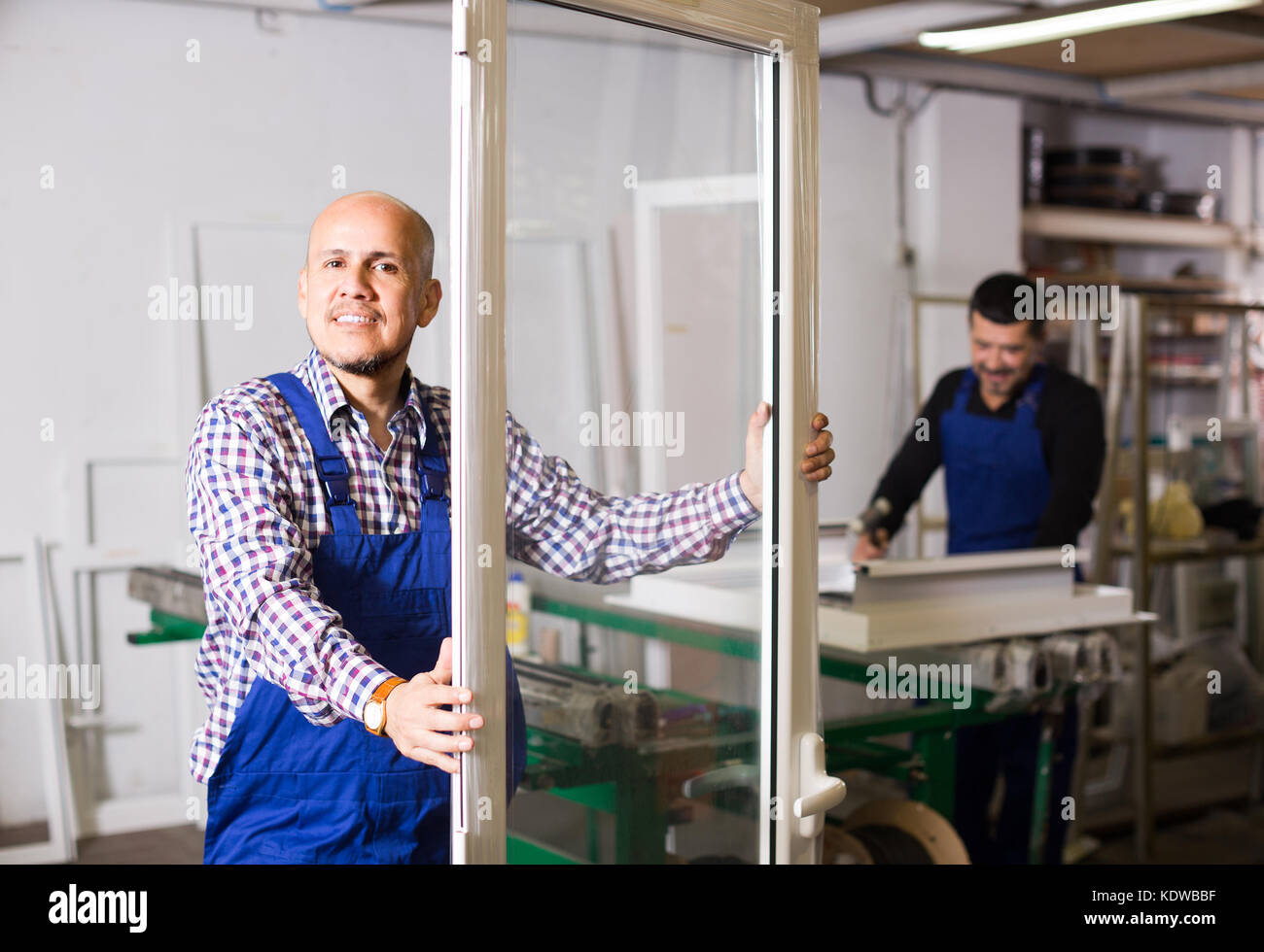 Two smiling workers in coveralls toiling with PVC window and door ...