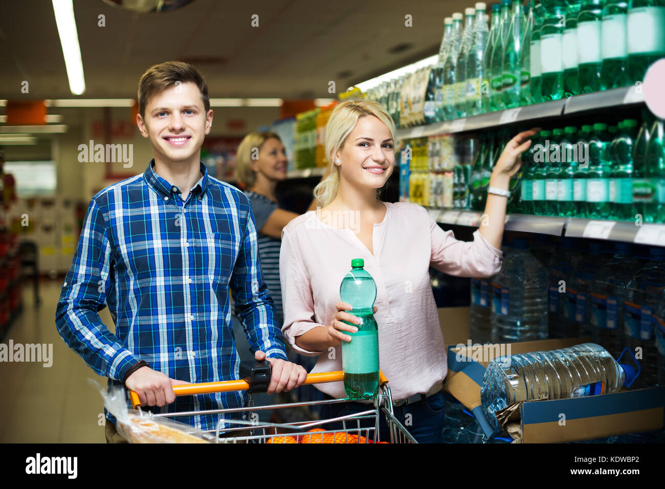 Young happy customers choosing bottle of sparkling water at store ...