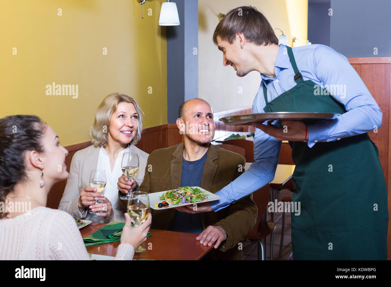 Young waiter serving table in restaurant with happy adults Stock Photo ...