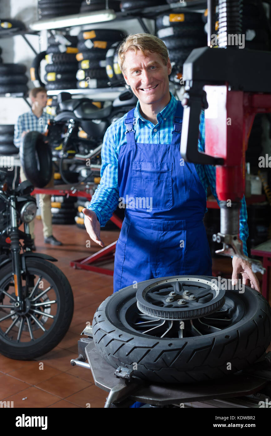 portrait of smiling mechanic man in uniform working with bike wheel in ...
