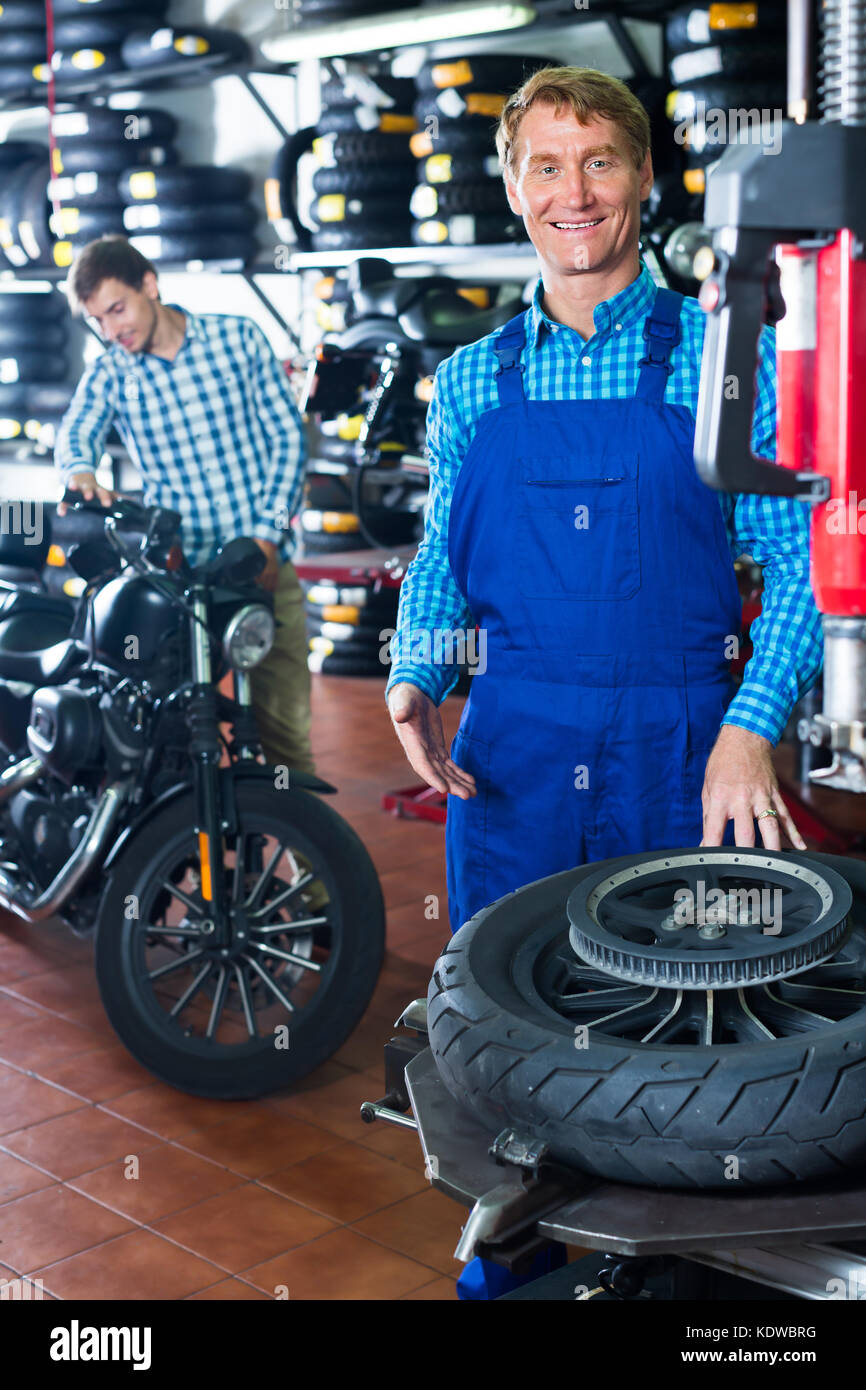 Attentive glad mechanic man standing with motorcycle wheel in shop Stock Photo - Alamy