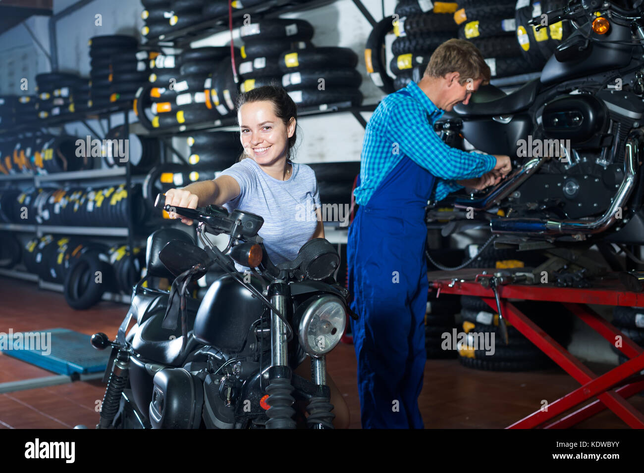 Young smiling woman customer sitting on motorcycle at service point ...