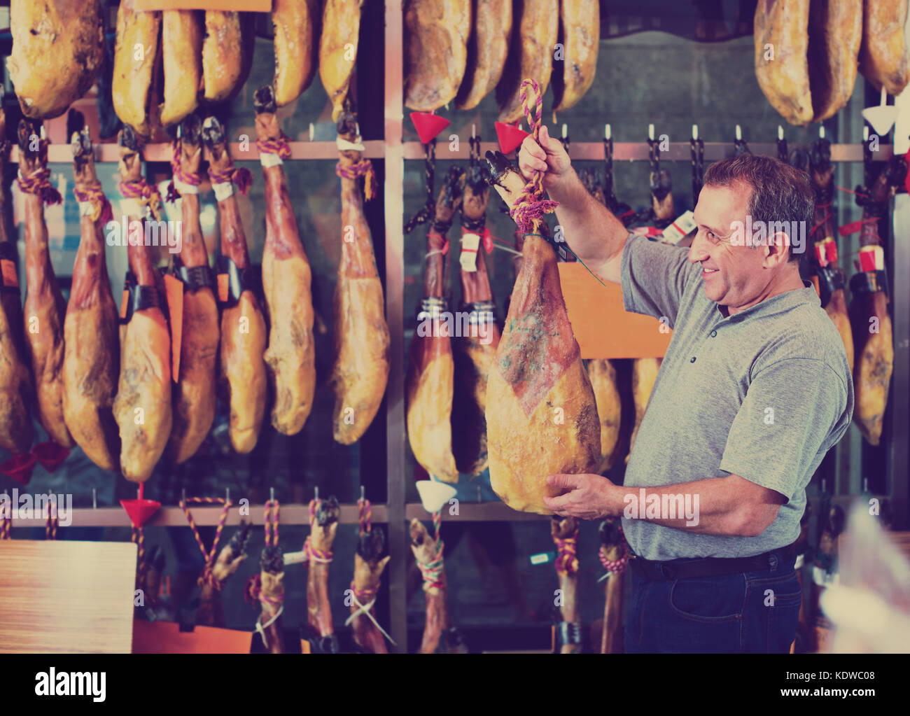 Cheerful mature customer buying iberico or serrano jamon leg in deli ...
