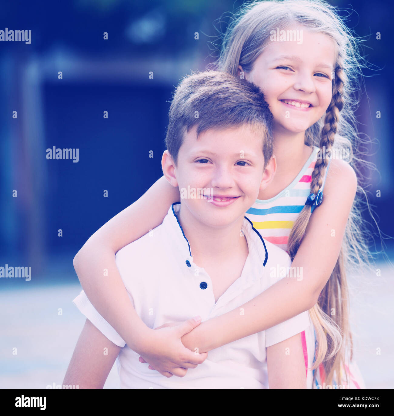 Two smiling kids in elementary school age hugging each other in town ...