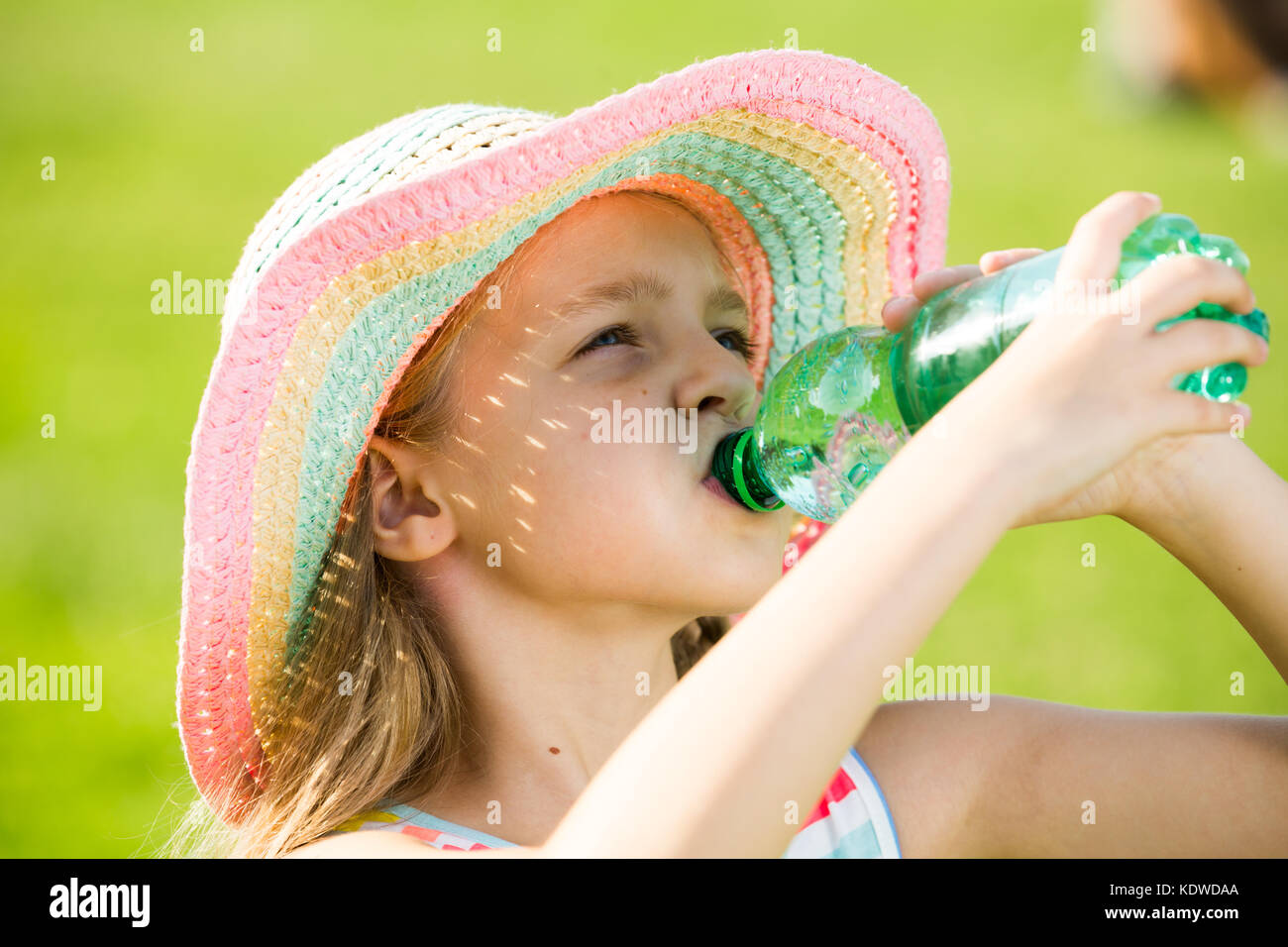 portrait of glad girl wearing sun hat drinking water in green park on ...