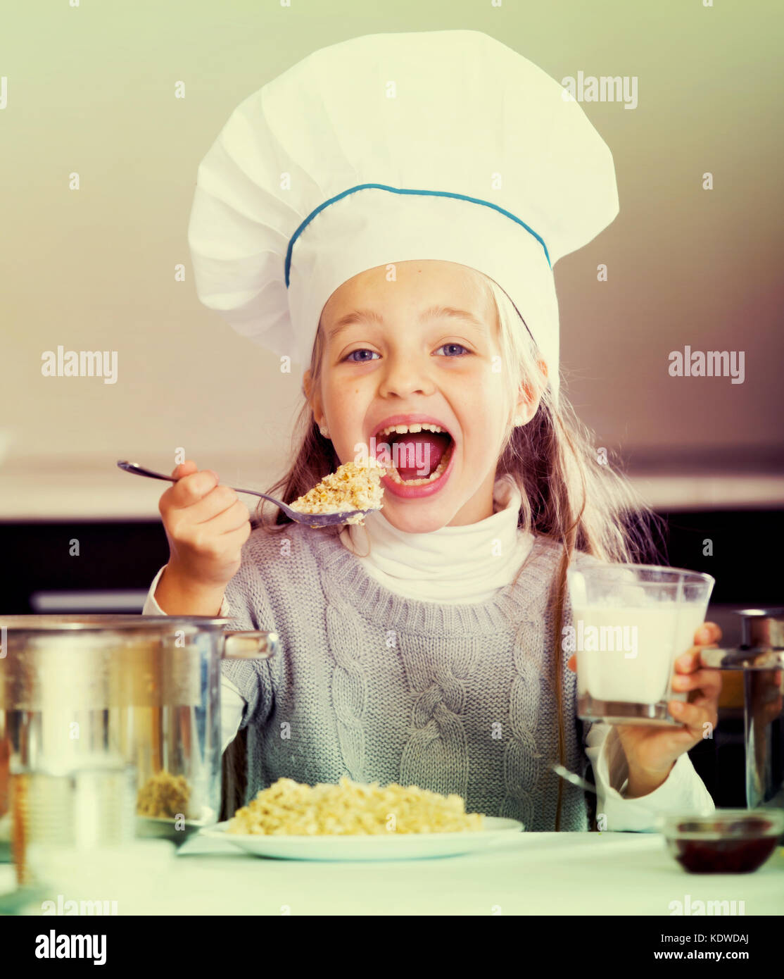Cheerful girl in cook cap eating porridge and drink milk Stock Photo ...